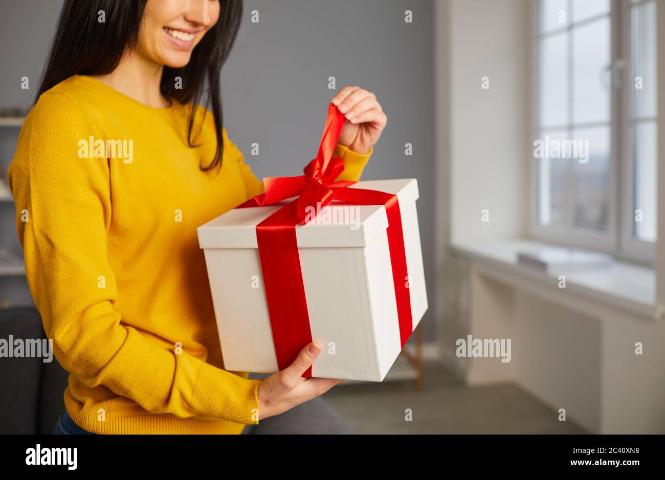 Happy girl with a gift box with a red ribbon sitting in the room Stock ...