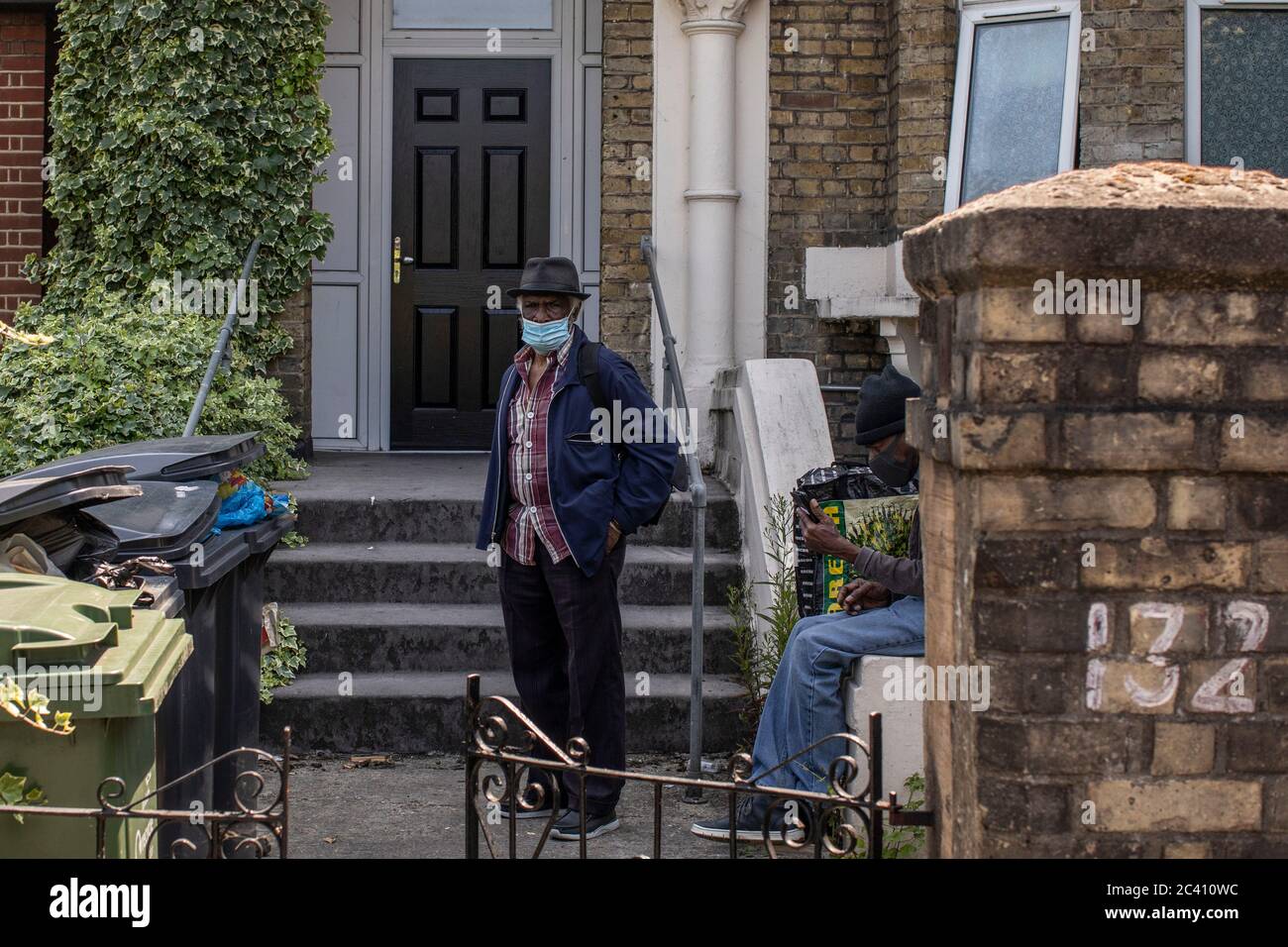 London, England. 23rd June 2020. Two men wearing face masks wait for a ...