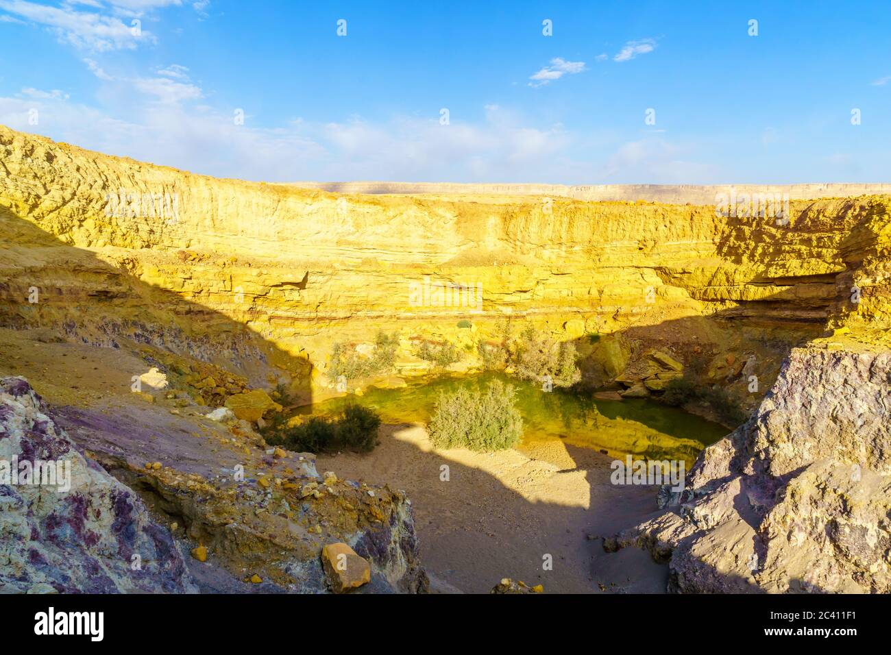 View of a water hole and layered rock formation, along the Ramon Colors ...