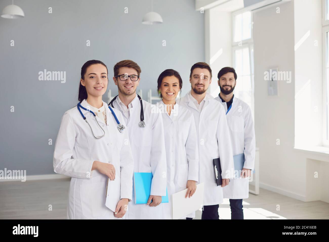 A group of confident practicing doctors in white coats are smiling ...