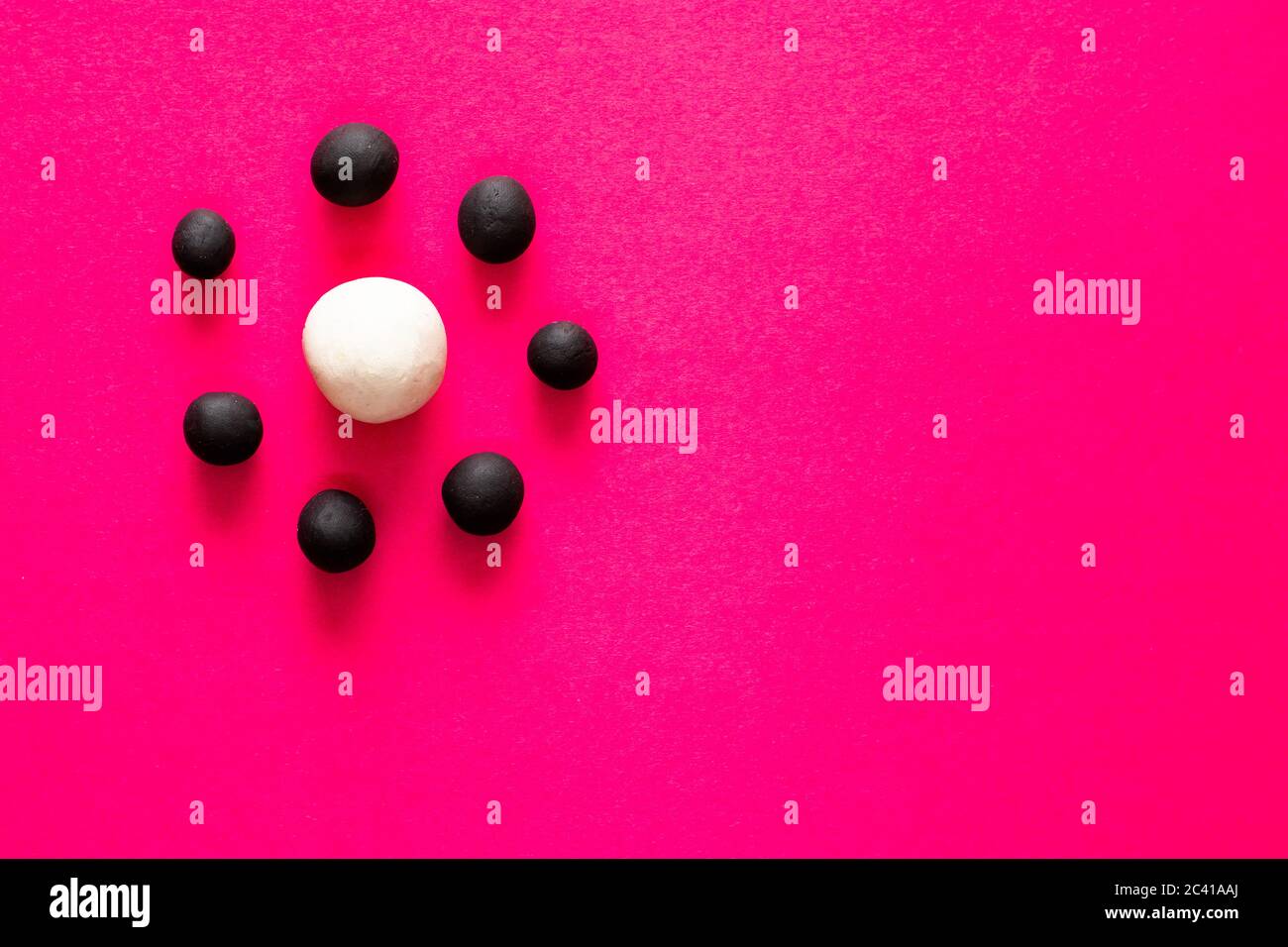 Small black balls surrounding a large white plasticine ball on pink ...