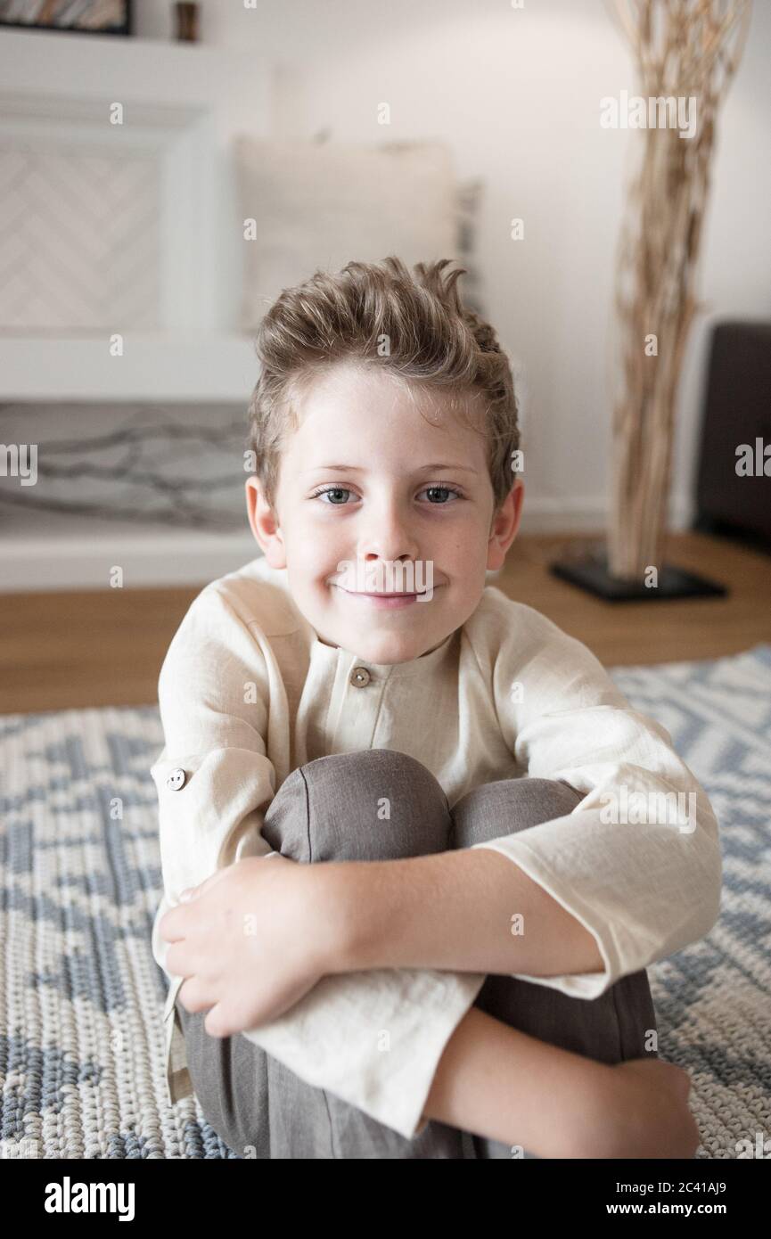 Cute boy in linen home clothes looks at a camera sitting on floor Stock ...
