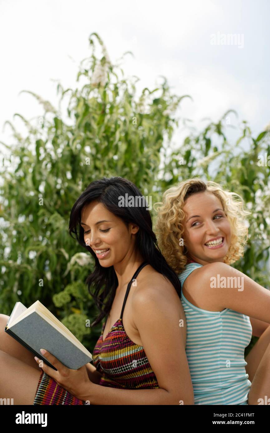 Two young women lean back to back - leisure time - girlfriends Stock ...