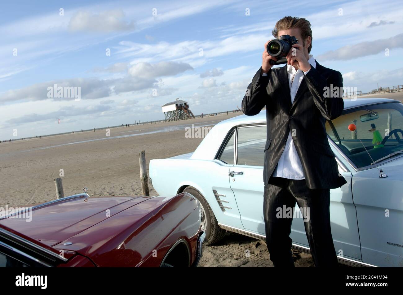 Man in a suit stands in front of two classic cars and takes photos ...