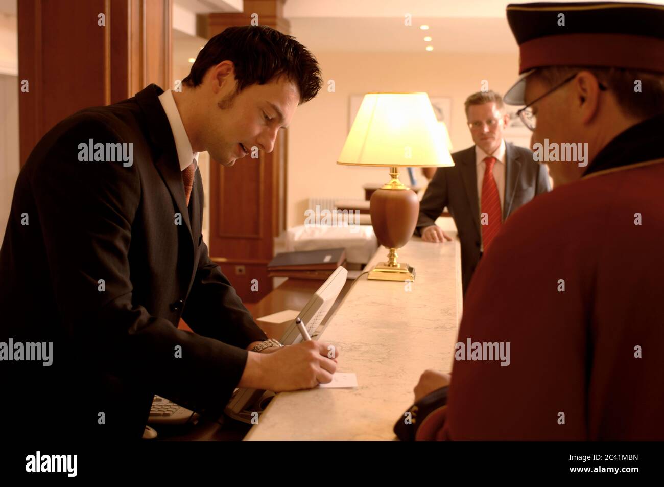 Young receptionist writes a note for a page, guest in the background ...