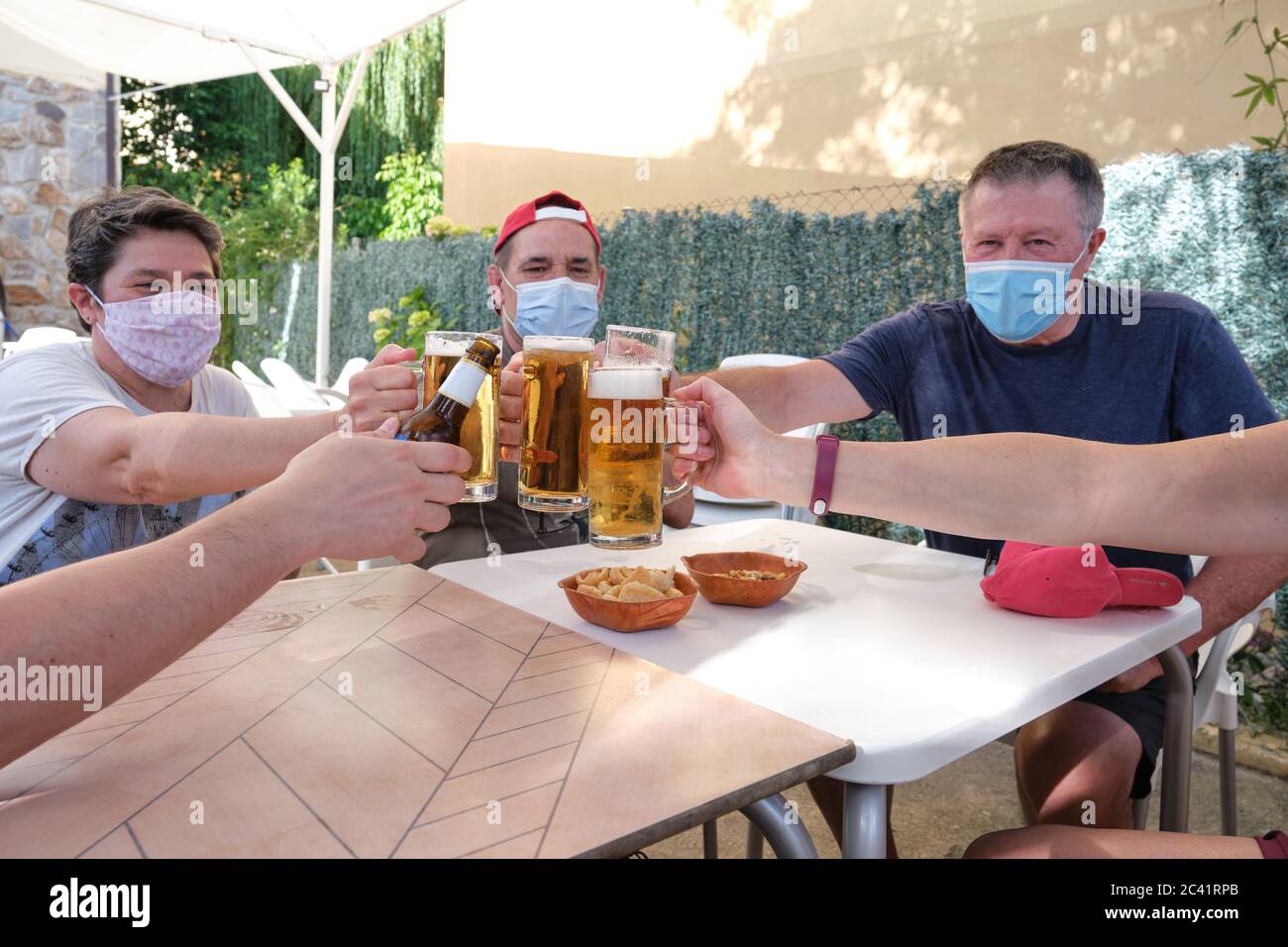 People with face masks cheering with beers in a bar. New normality in ...
