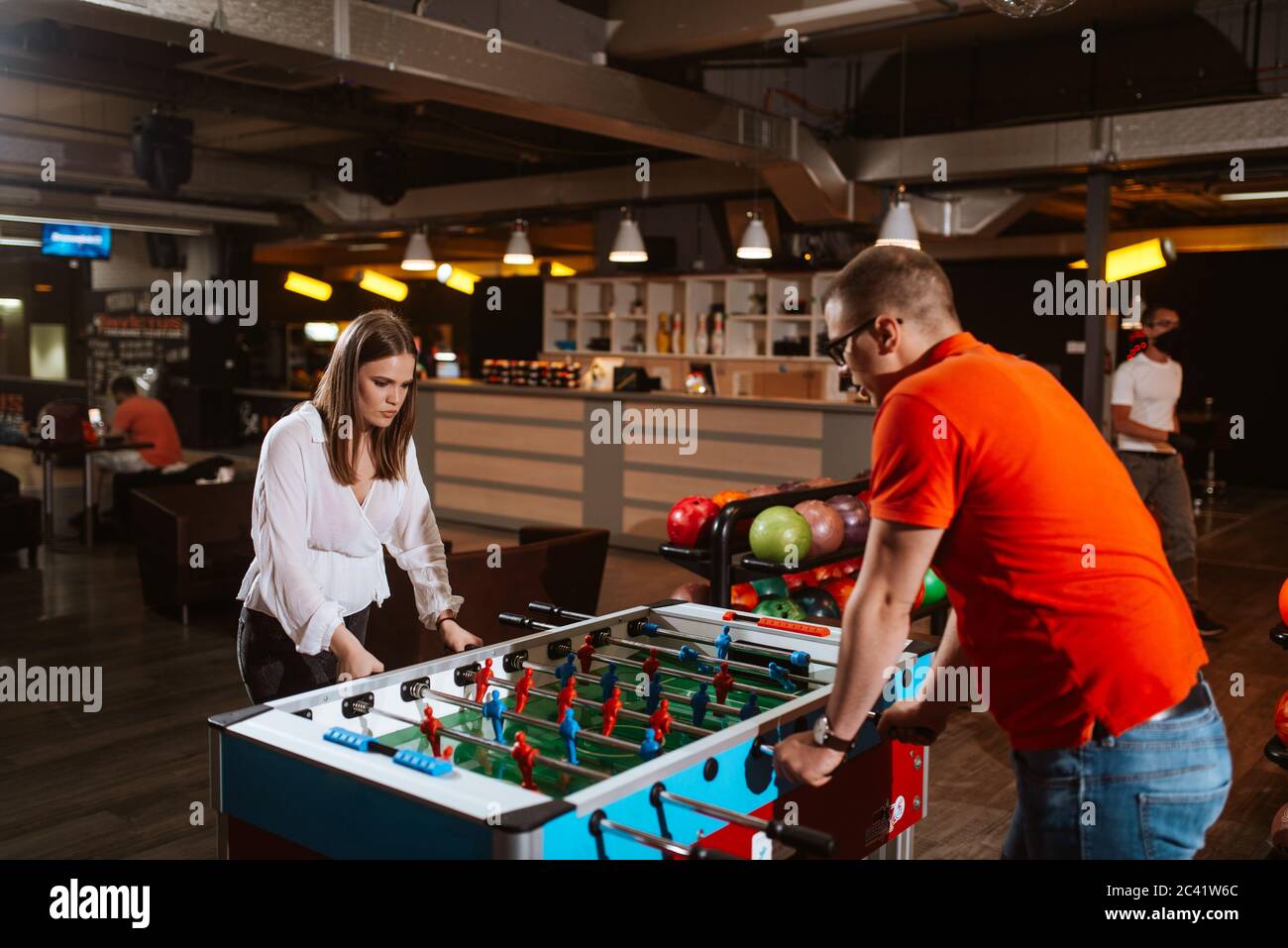 A beautiful caucasian girl and a man with glasses play table football ...