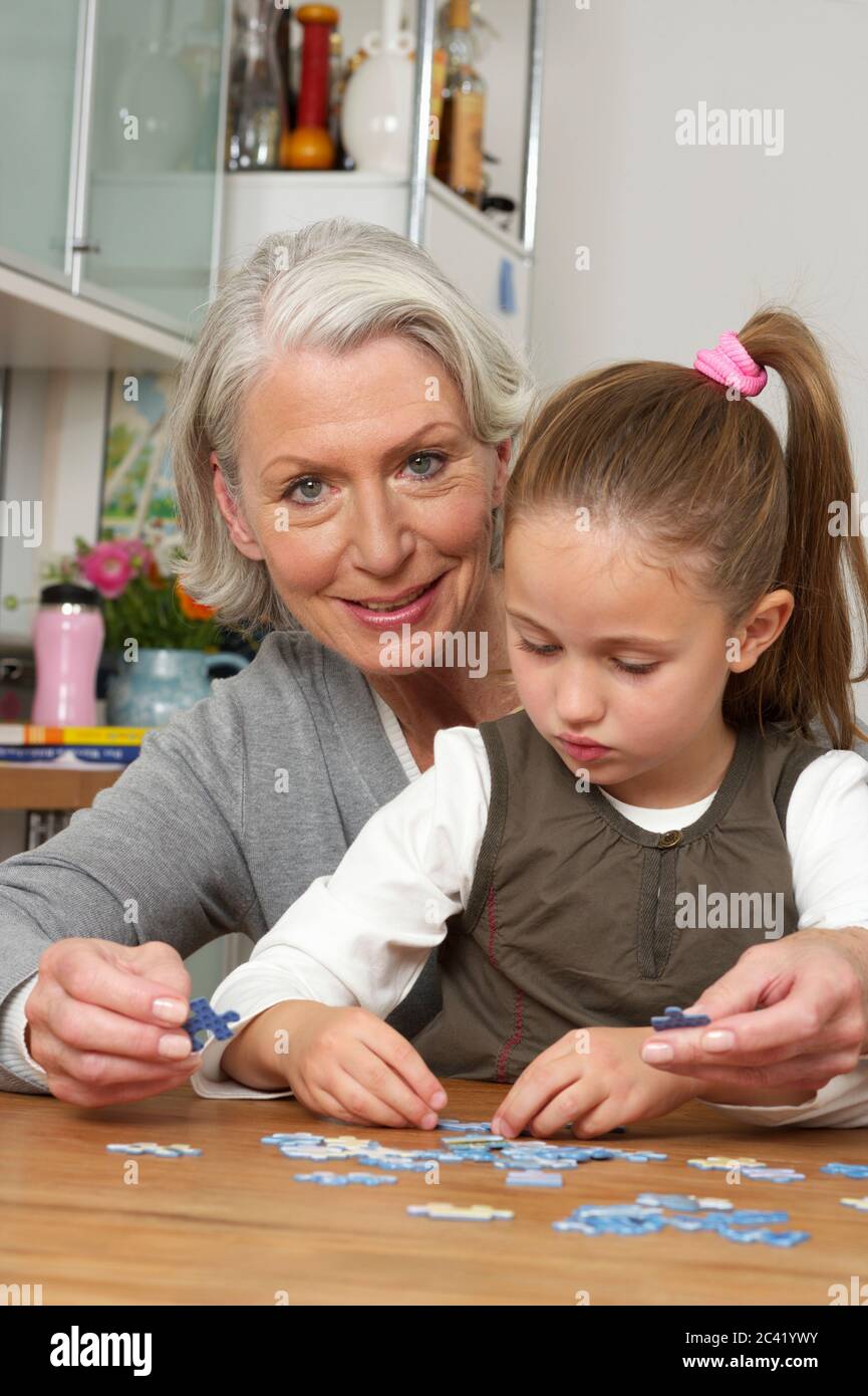 Grandma sits at a table with her granddaughter and does a puzzle with ...