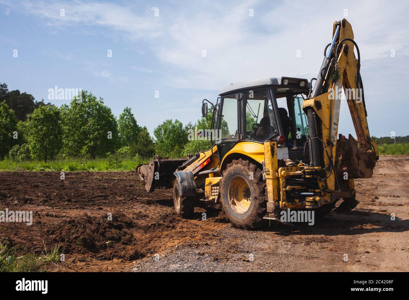 Clearing and leveling a private land plot. Yellow excavator driven ...