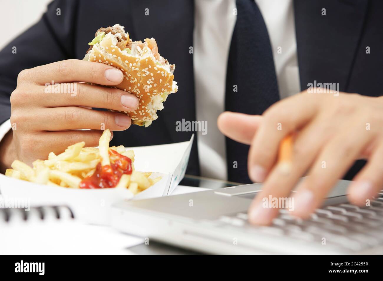 A man in a suit eats a burger and types on a notebook - restaurant ...