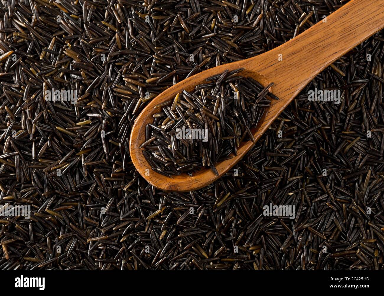 Heap of uncooked, raw, black wild rice grains in wooden scoop on rice ...