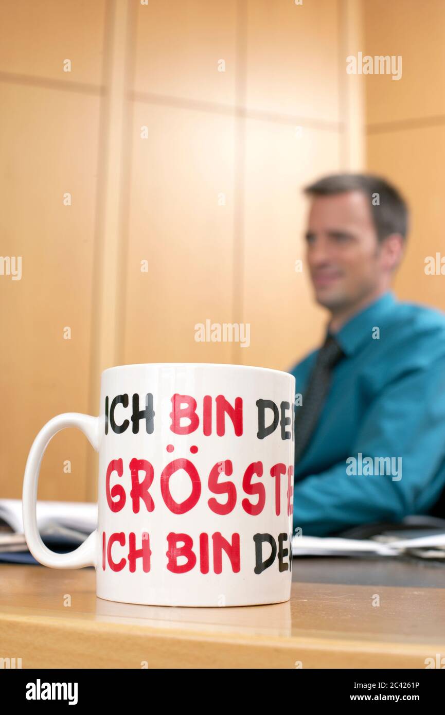 Businessman at his desk with a huge motto mug in front of him - boss ...
