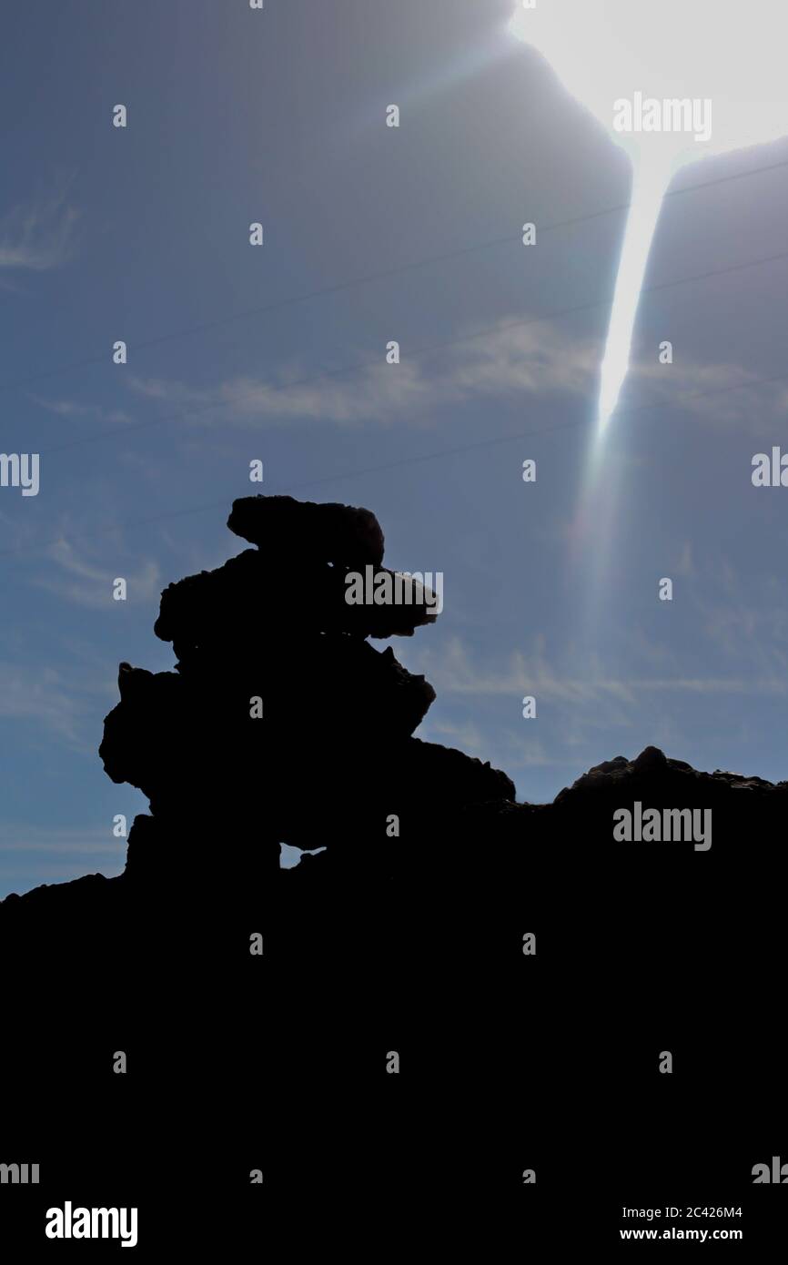 Silhouette of a pile of rocks against a blue sky with the sun in the ...