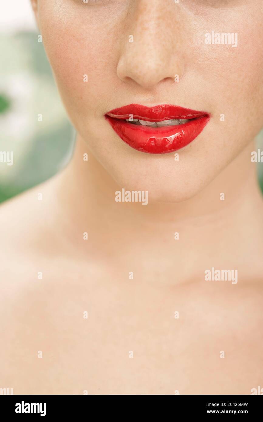 Lower half of the face of a young woman with red painted lips ...
