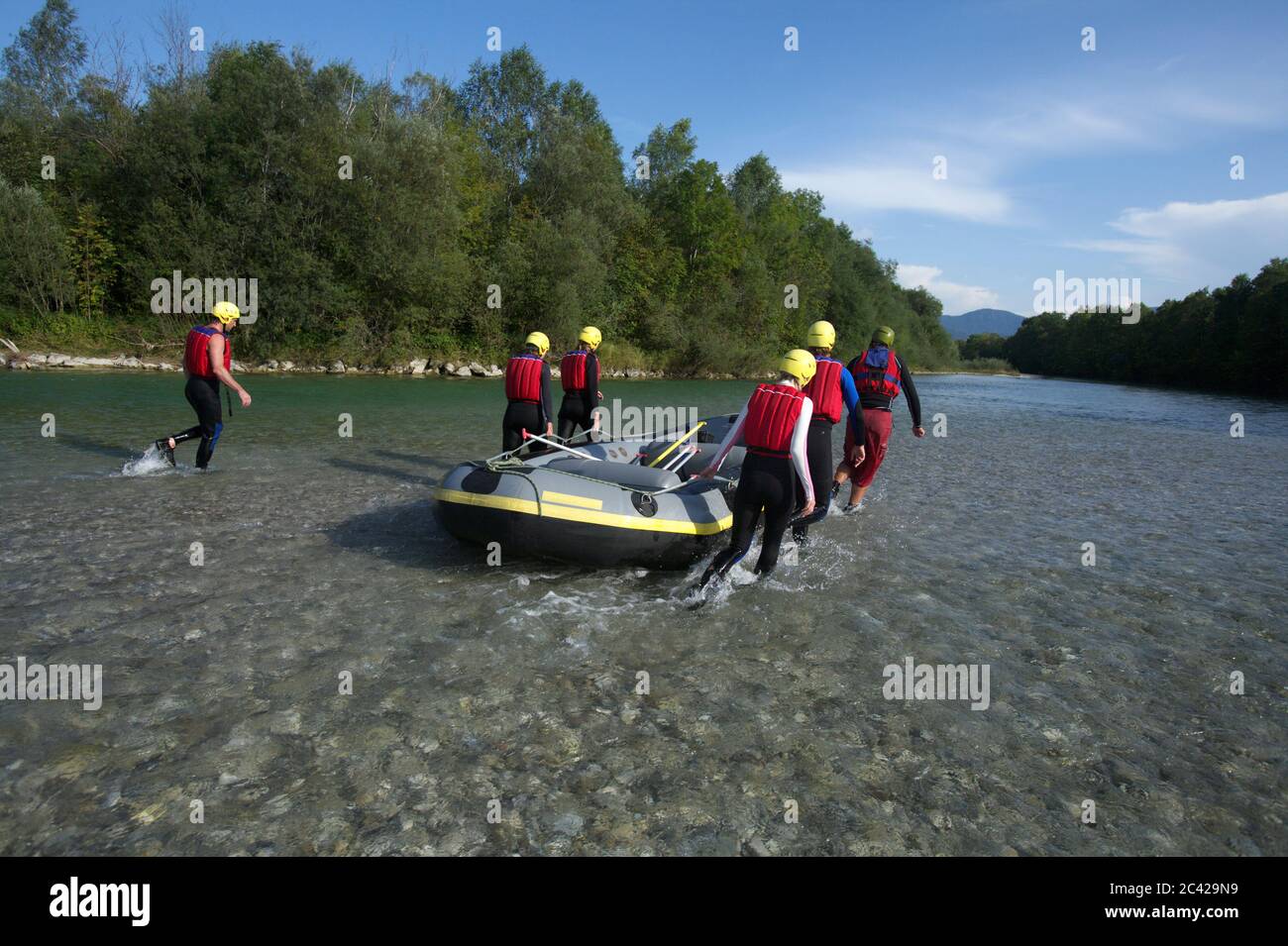 A group of six young people push an inflatable raft into the river ...