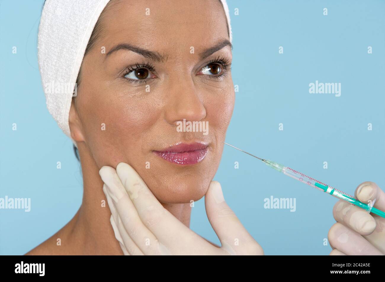 Gloved hand with an injection needle in front of a woman's face ...