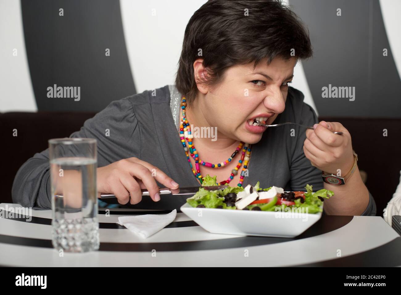 Young vigorous woman reluctantly eats a salad diet grimace problem ...