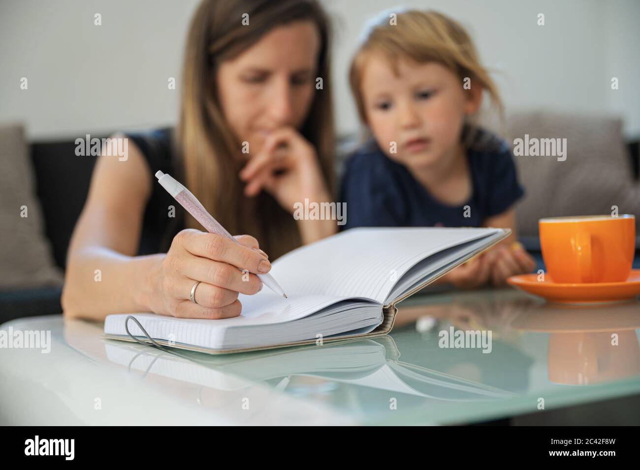 Young student mother studying from home, making notes in notebook with ...