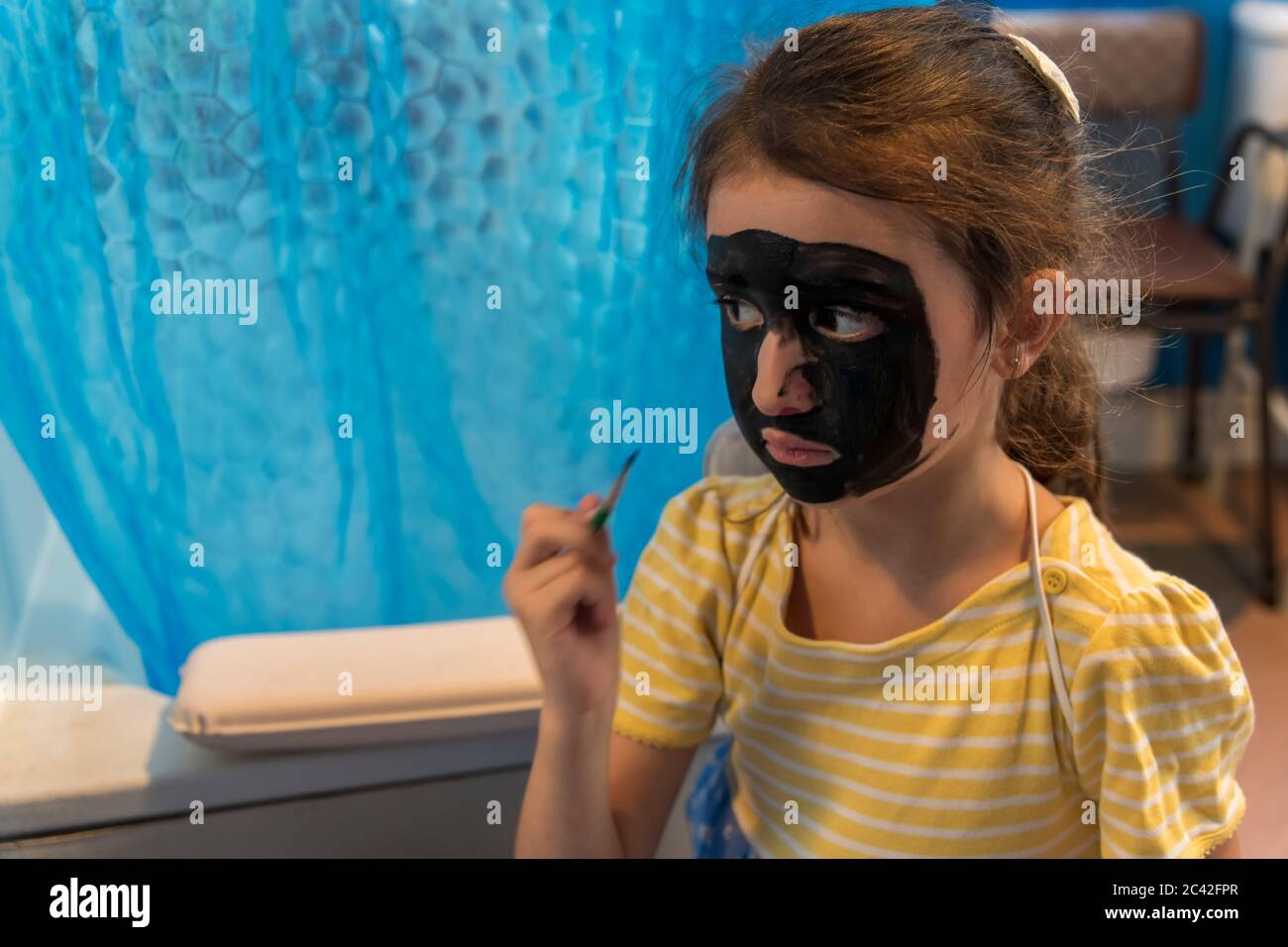 A young girl from poor deprived family is entertaining herself by face ...