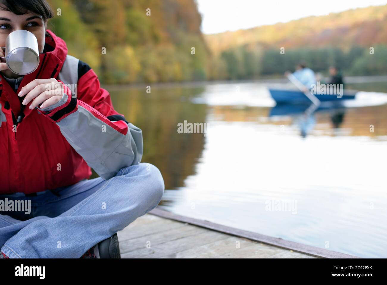 Woman sits on a wooden jetty and drinks Stock Photo - Alamy