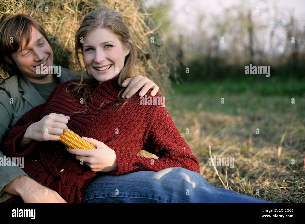 Couple is sitting in front of a haystack Stock Photo - Alamy