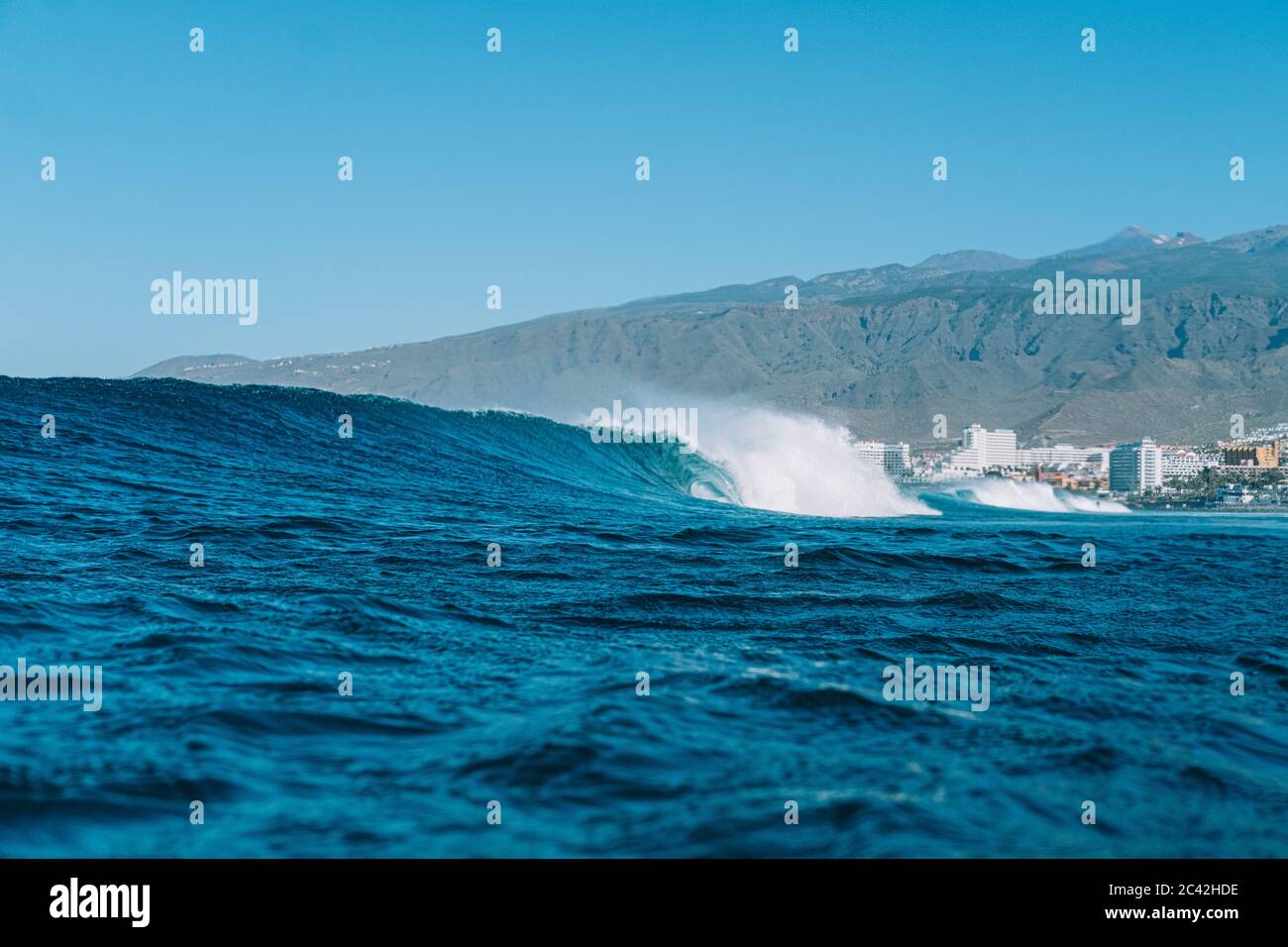 Pulled back view of a wave with mountains in the back Stock Photo - Alamy
