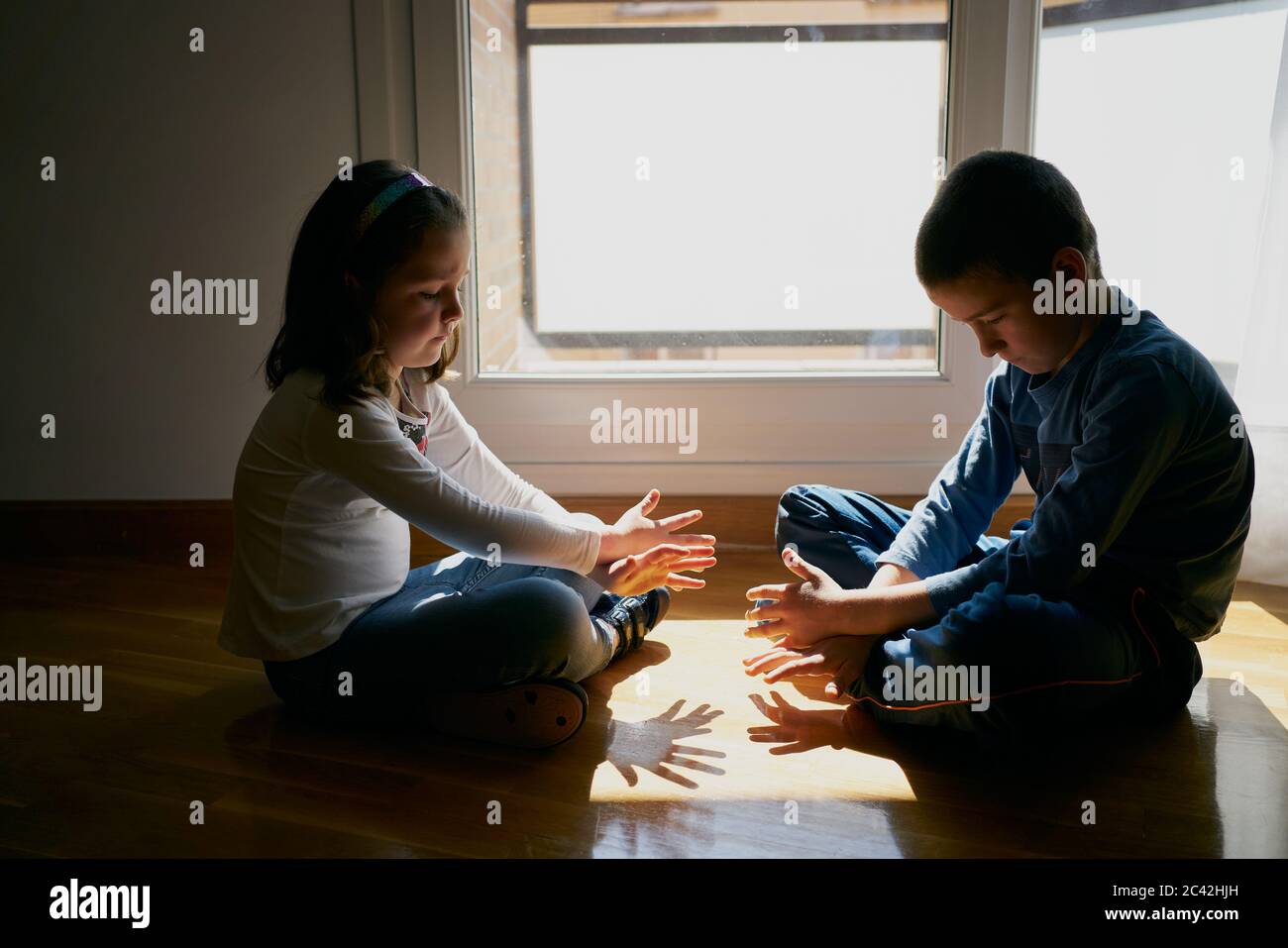 two children sitting on the floor playing with their hands in shadows ...