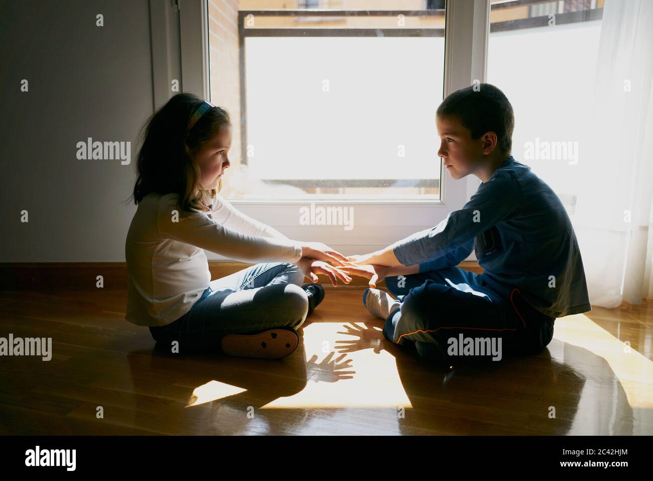 two children sitting on the floor playing with their hands in shadows ...