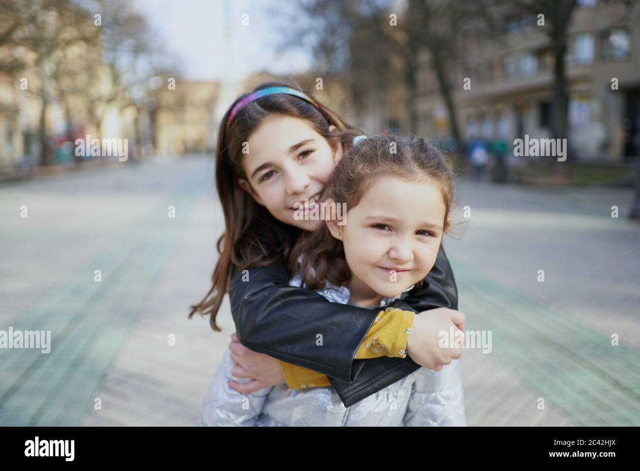 two happy girls look at a smiling camera in the middle of a city walk ...