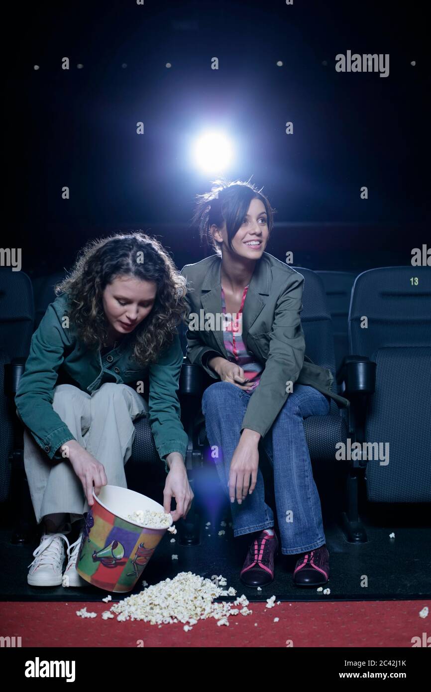 Two young women in the cinema pick up overturned popcorn from the floor ...