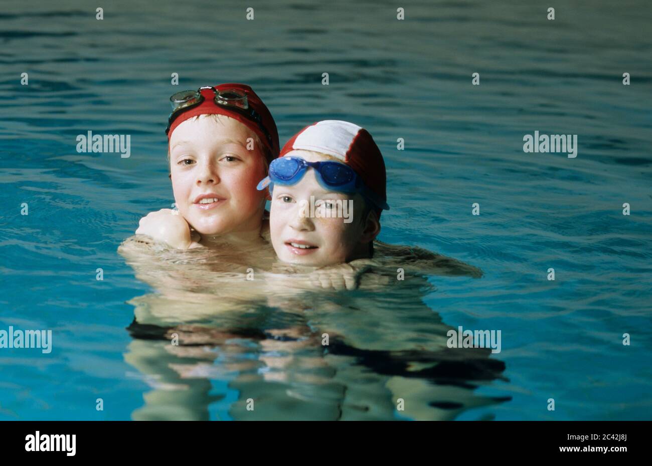 Two boys swim next to each other with a bathing cap and diving goggles ...