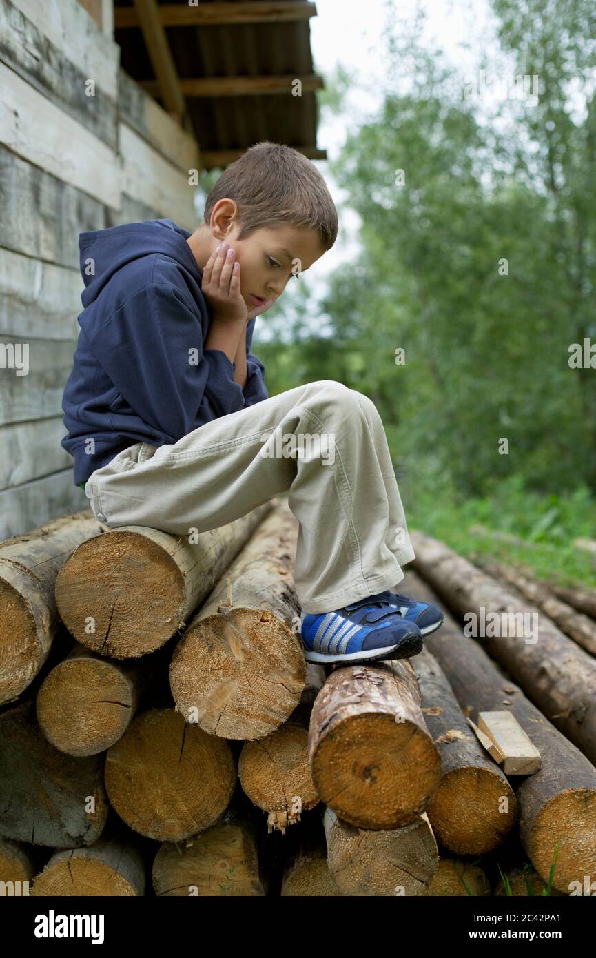 A boy sits on a log pile Stock Photo - Alamy