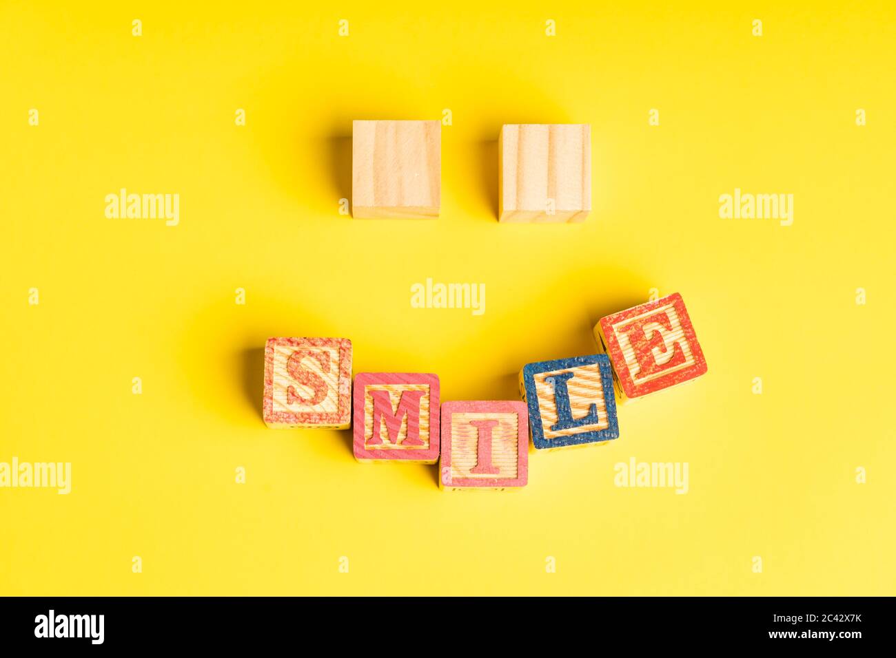 wooden blocks forming a smiling face against yellow background with ...