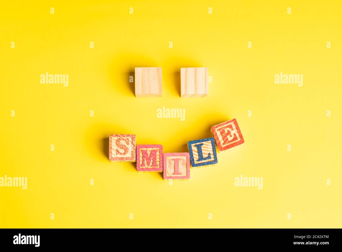 wooden blocks forming a smiling face against yellow background with ...