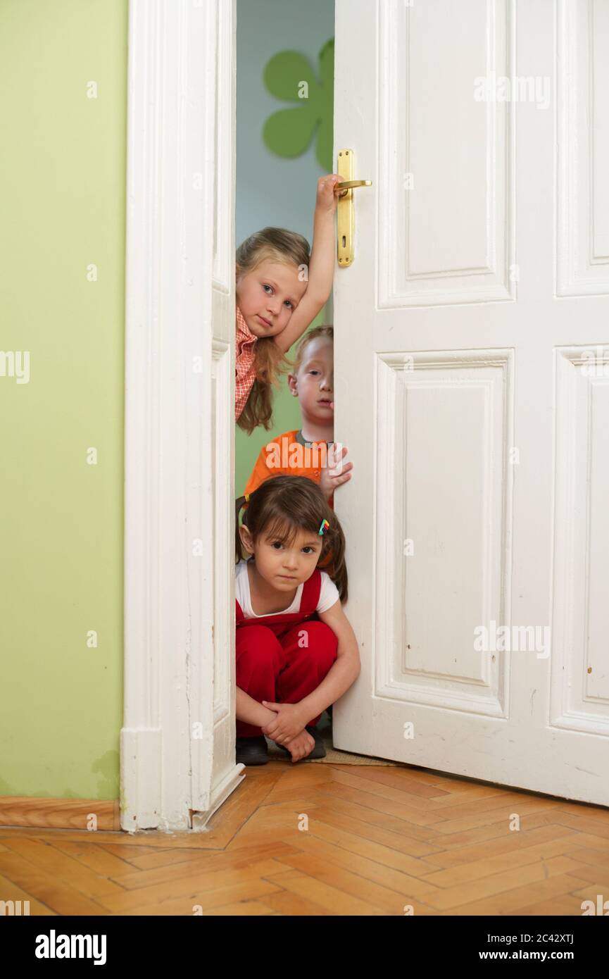 Three children (4-5 years) look through a crack in the door Stock Photo ...