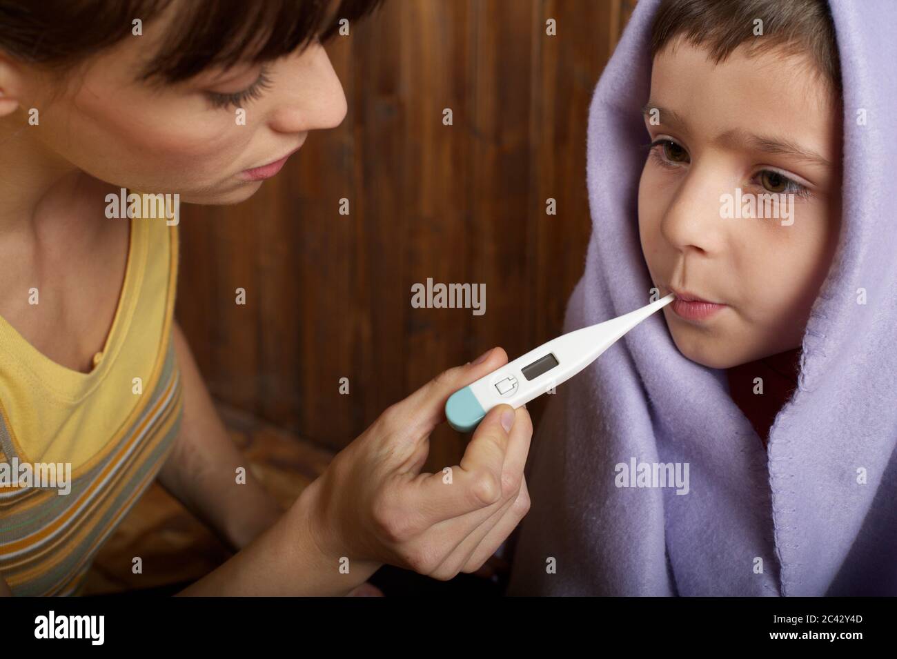Brunette woman measures fever in a child wrapped in a blanket - cold ...