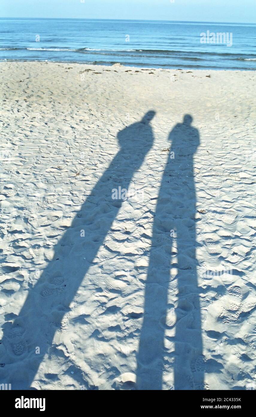 Two people cast shadows on sandy beach Stock Photo - Alamy