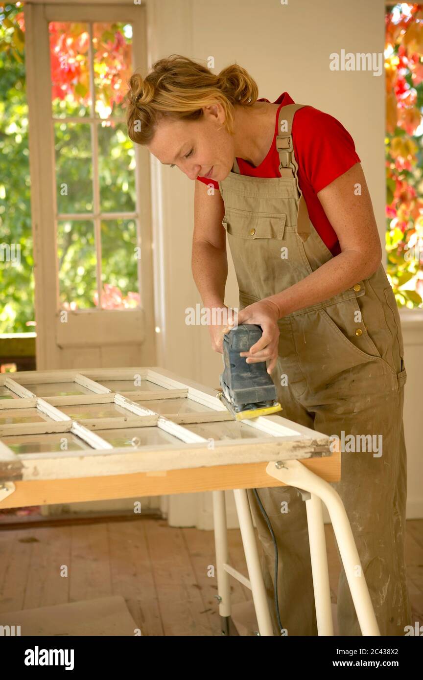 Young woman with work clothes grinds a window frame with a grinder ...