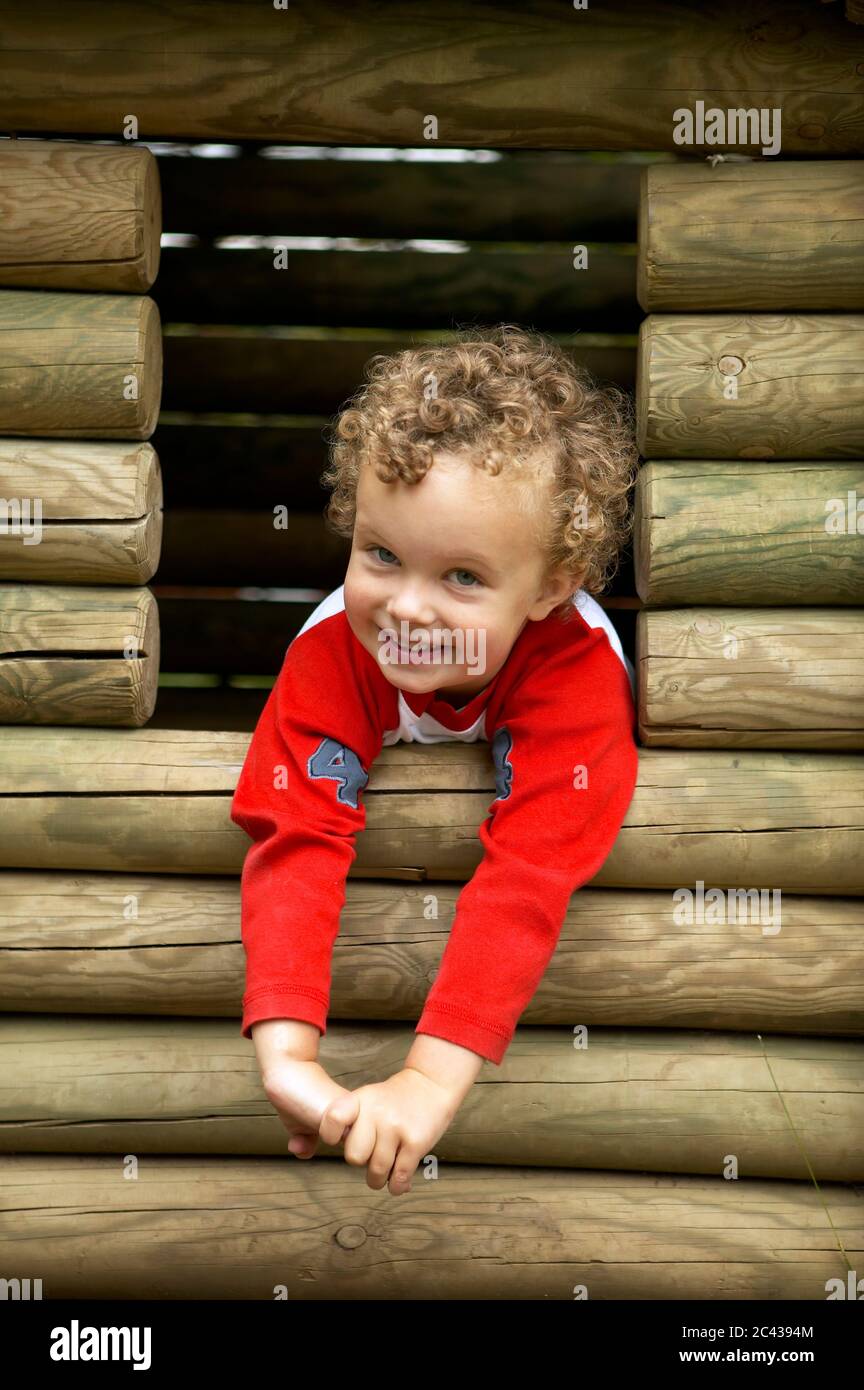 Hilarious little child looks out of wooden house window Stock Photo - Alamy