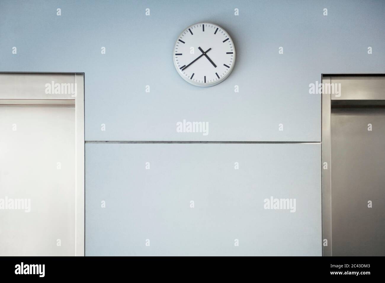 Clock between two elevator doors Stock Photo - Alamy