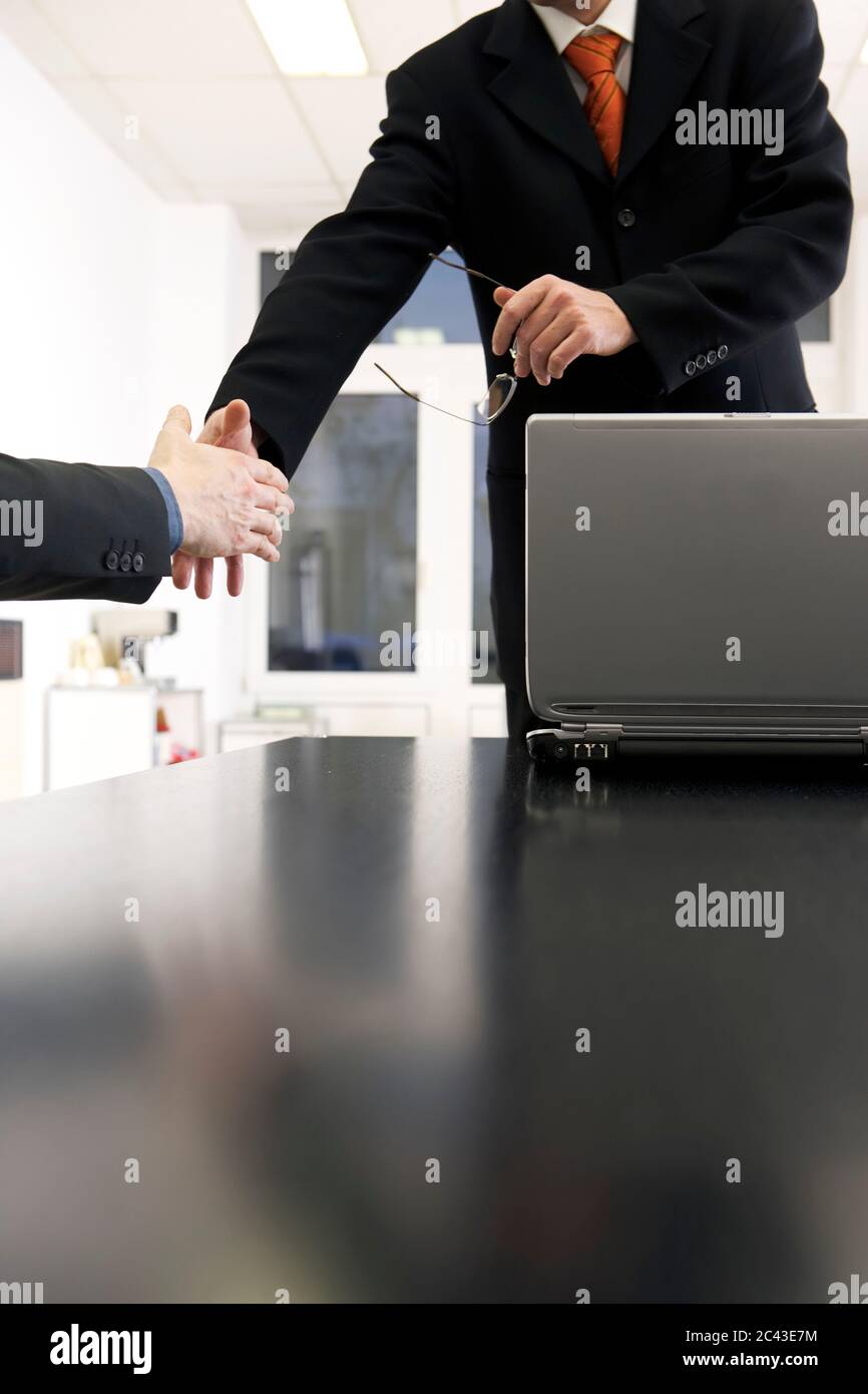 Businessman stands at a conference table and shakes someone's hand ...