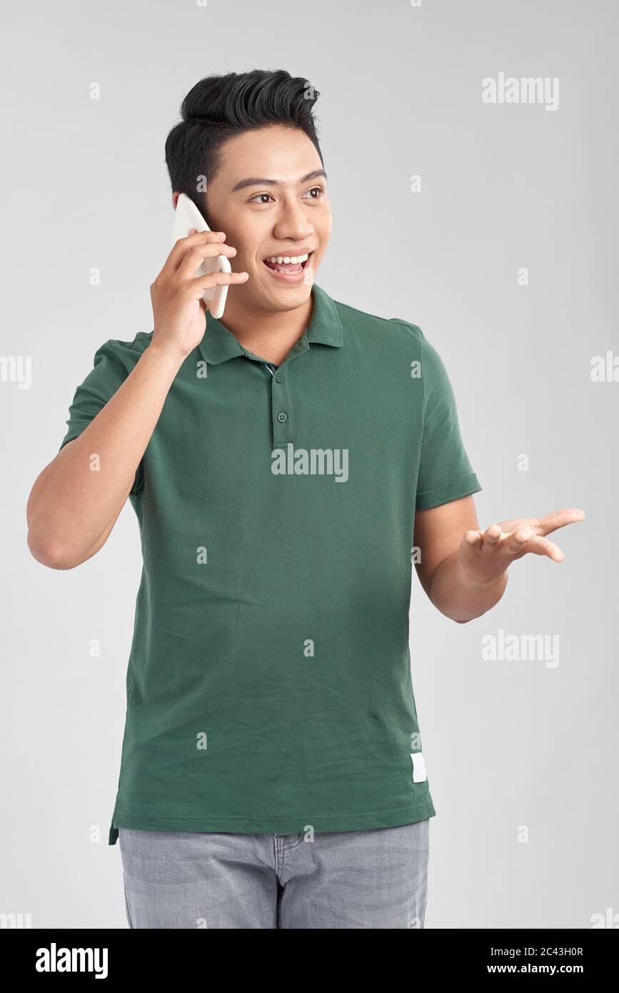 Cheerful casual man talking on phone and celebrating standing on white ...