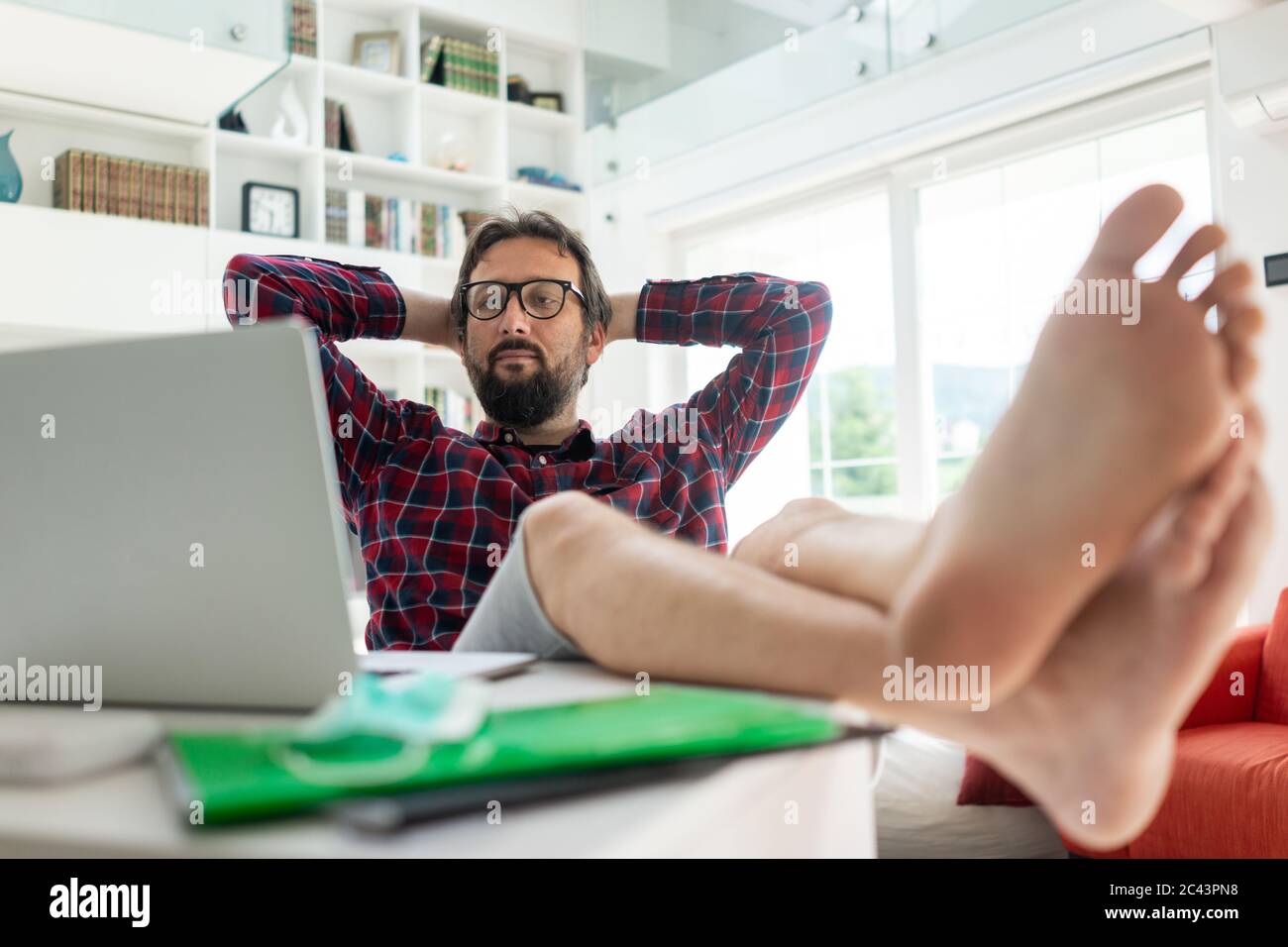 Man in home office working on laptop with legs on desk Stock Photo - Alamy
