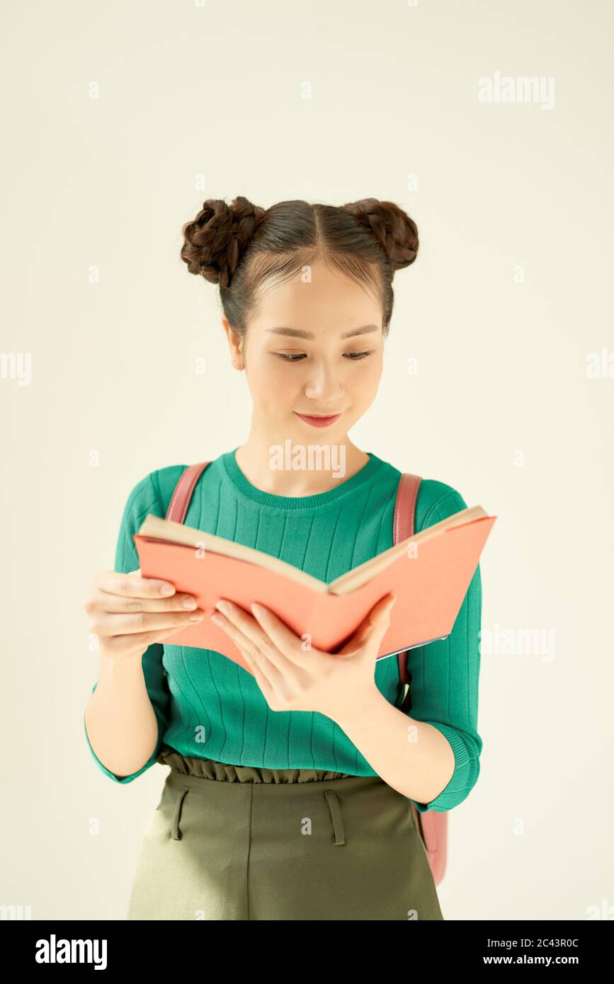 Portrait of a smiling female teenager with backpack reading book ...