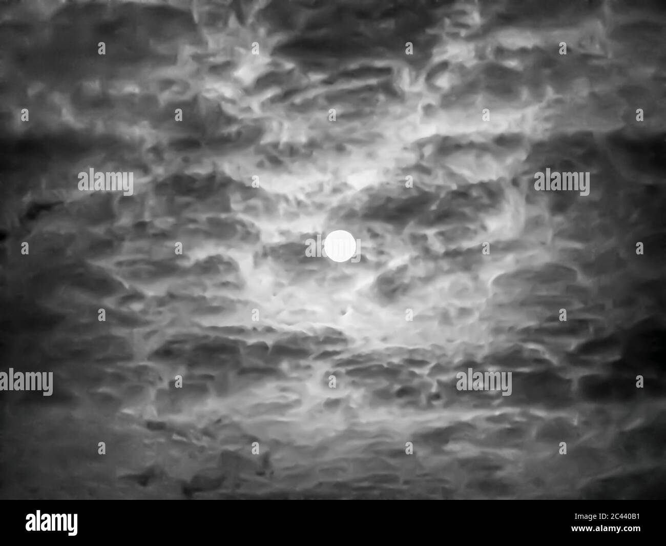 A thin layer of clouds covers a full moon. The reflected light from the ...