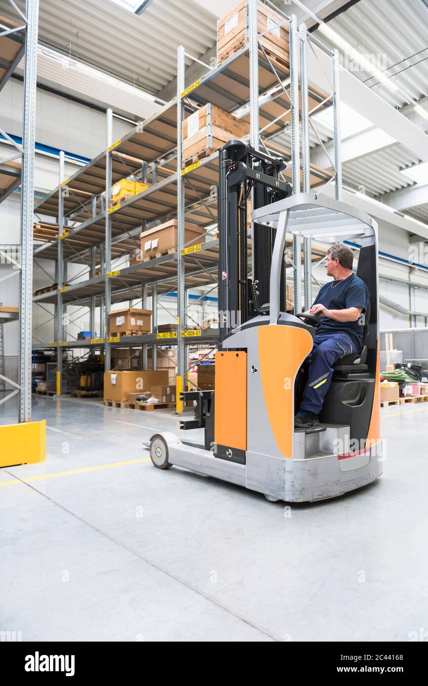 Worker on forklift in high rack warehouse Stock Photo - Alamy
