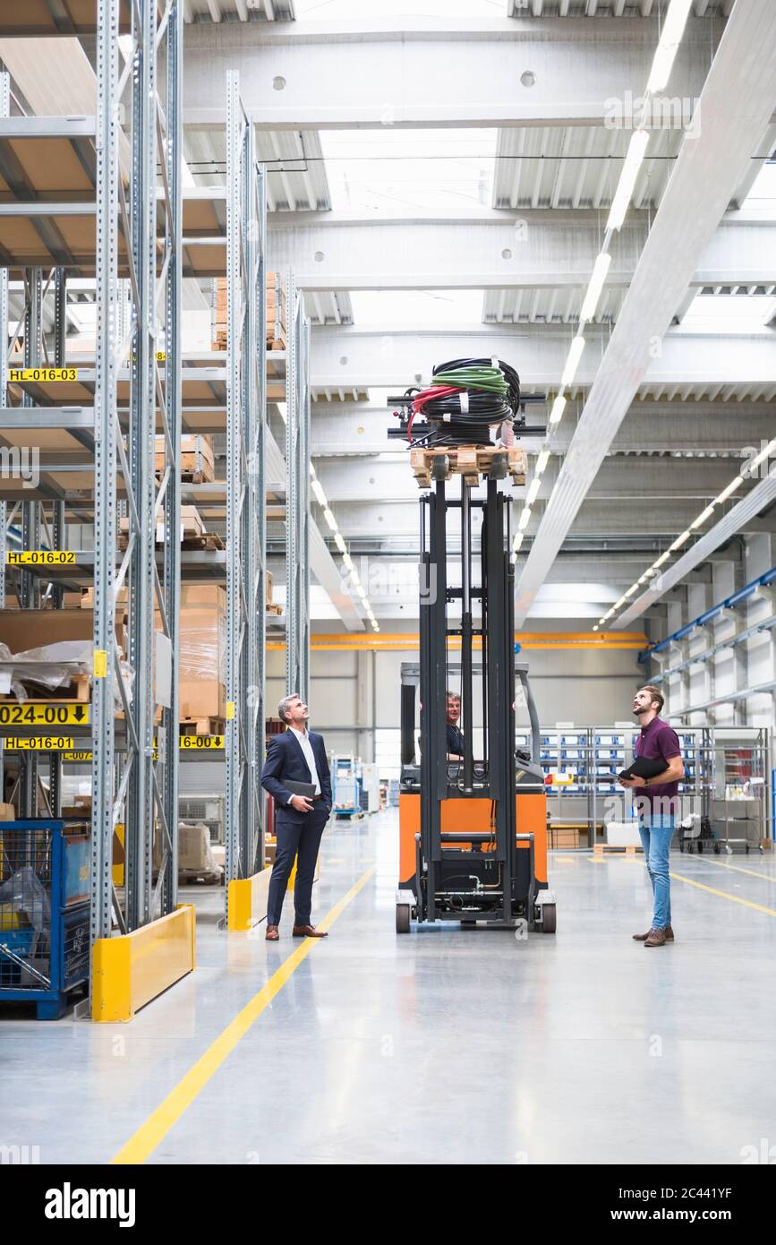 Two men and worker on forklift in high rack warehouse Stock Photo - Alamy