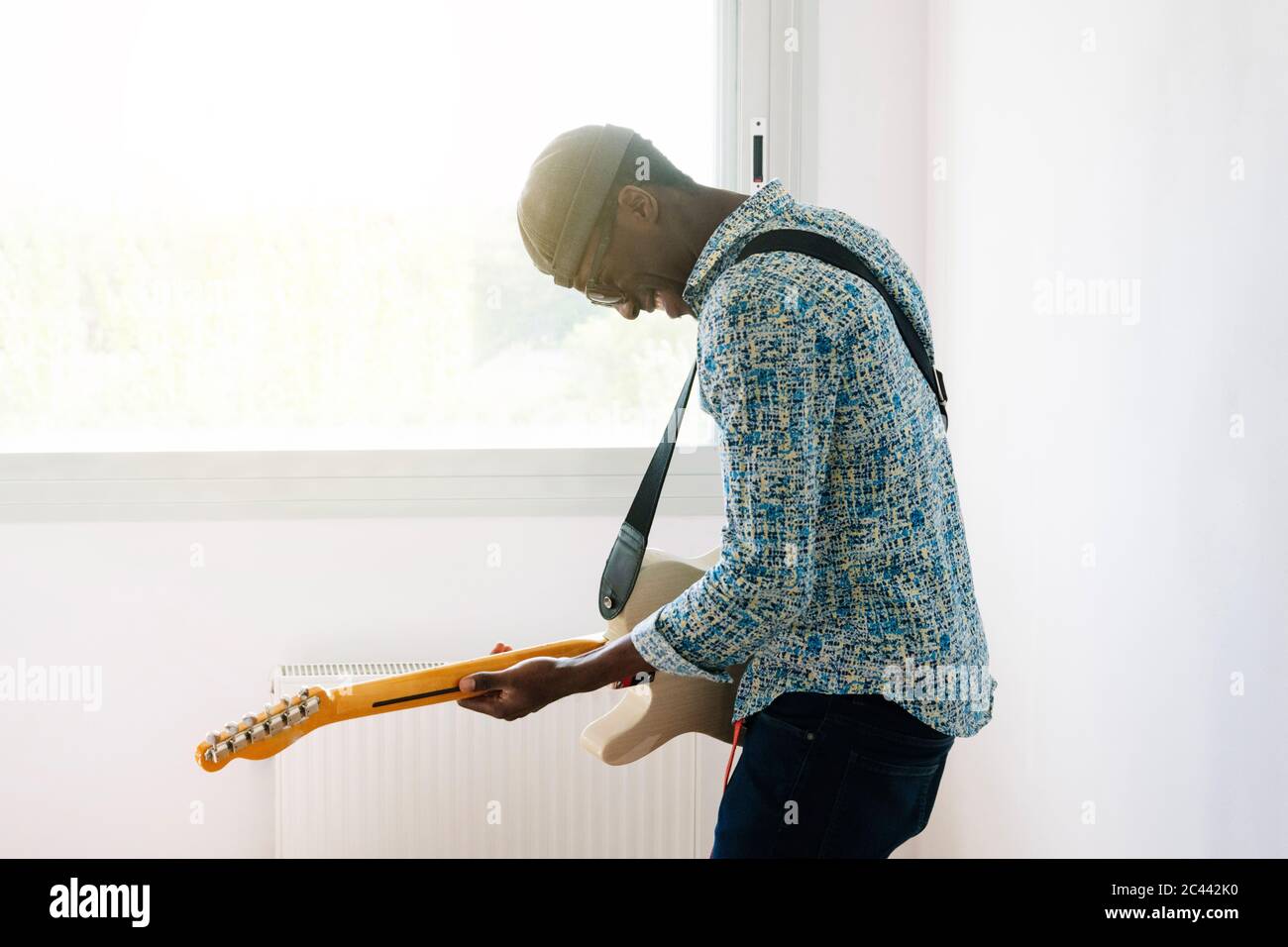 Smiling young pop musician playing guitar by window Stock Photo - Alamy