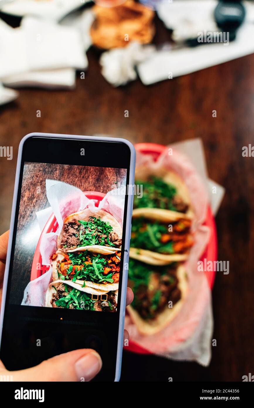 Hand of woman photographing tacos on table with smart phone in ...