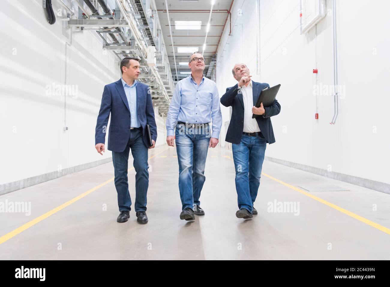 Three businessmen walking and talking on factory corridor Stock Photo ...